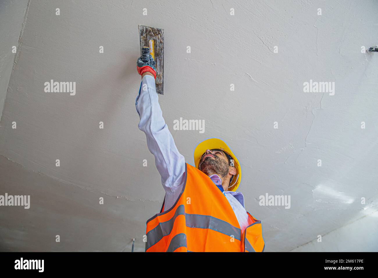 A plasterer in construction wears overalls and a hat. He is plastering ...