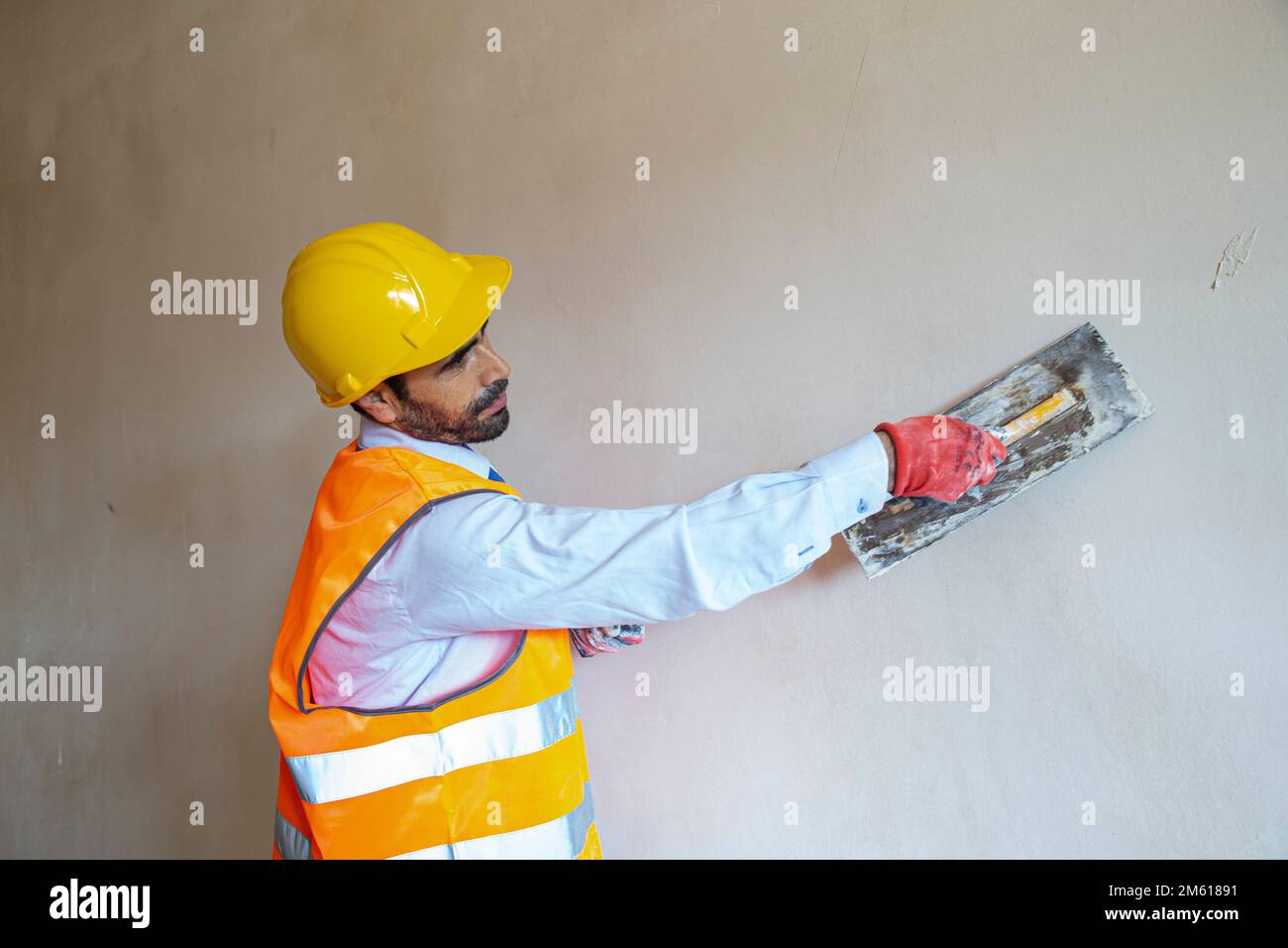 A plasterer in construction wears overalls and a hat. He is plastering ...