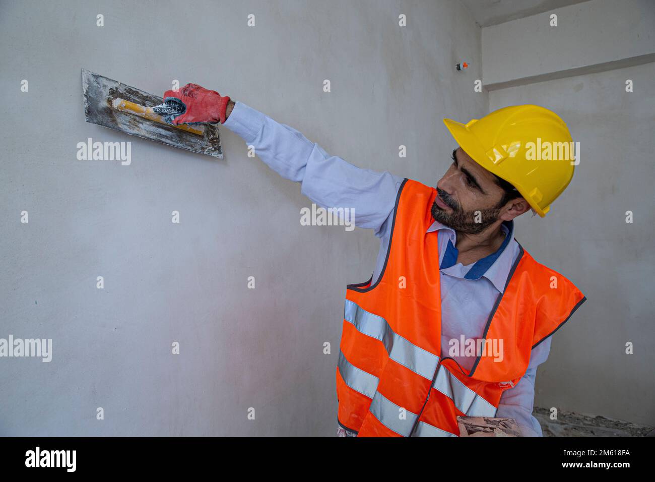 A plasterer in construction wears overalls and a hat. He is plastering ...