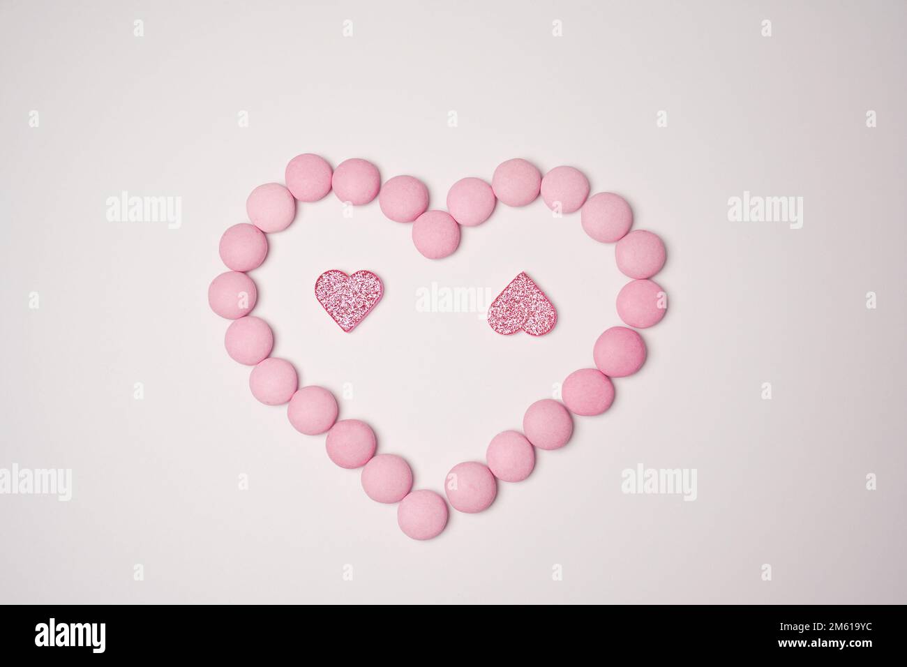 Sweets candies as heart with two glittering pink hearts on white ...