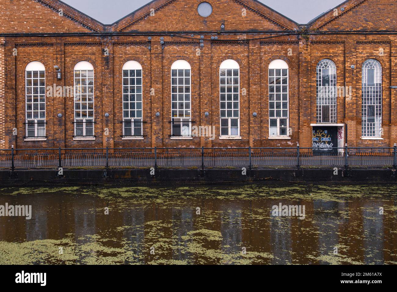 Detail of a row of old industrial buildings sitting alongside a river ...