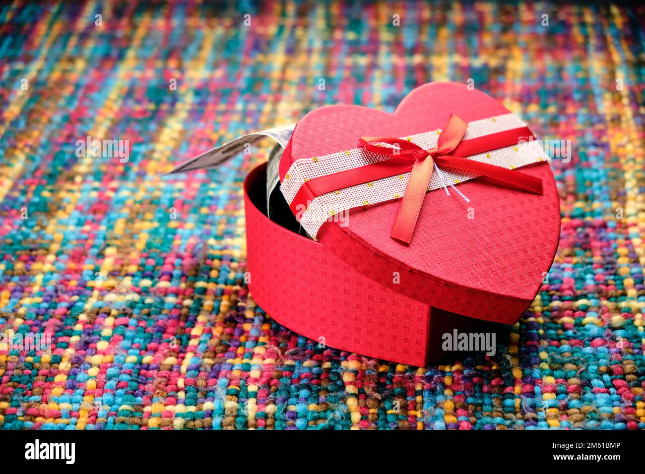 A gift in the shape of a half-open red heart with dollar notes peeking ...