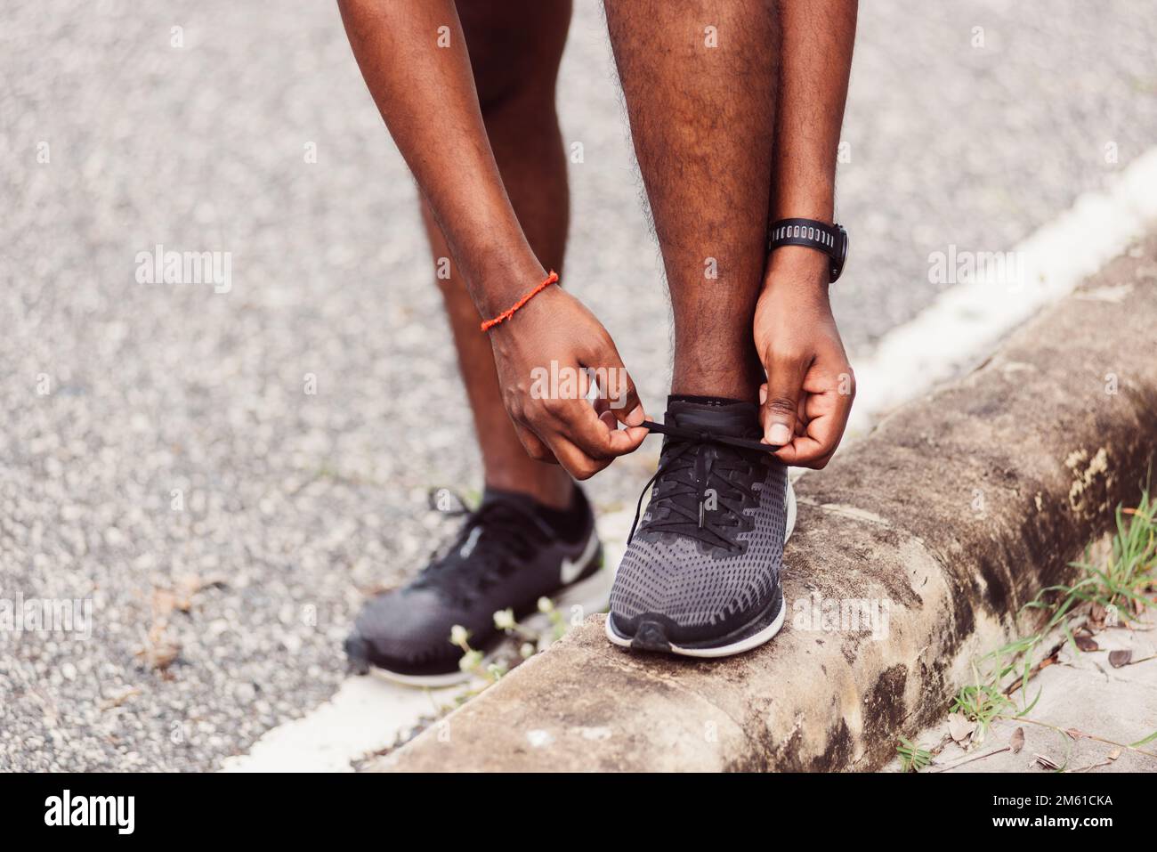 runner black man wear watch stand step on the footpath trying shoelace ...