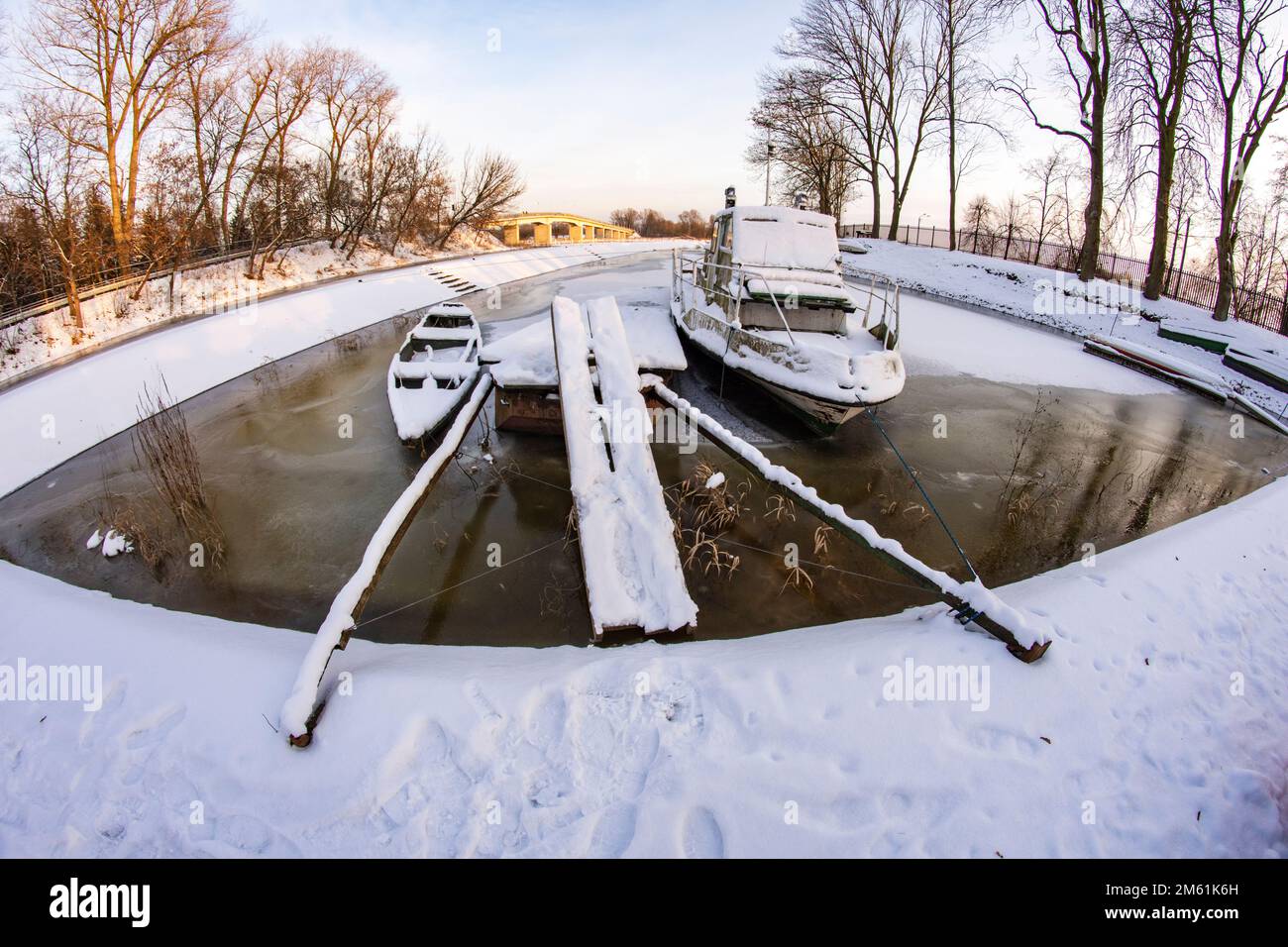 Yacht and jetty in a winter harbor covered in ice and snow, bridge and ...