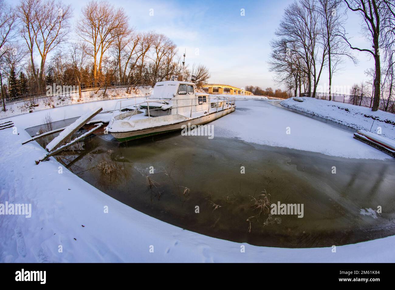 Yacht and jetty in a winter harbor covered in ice and snow, bridge and ...