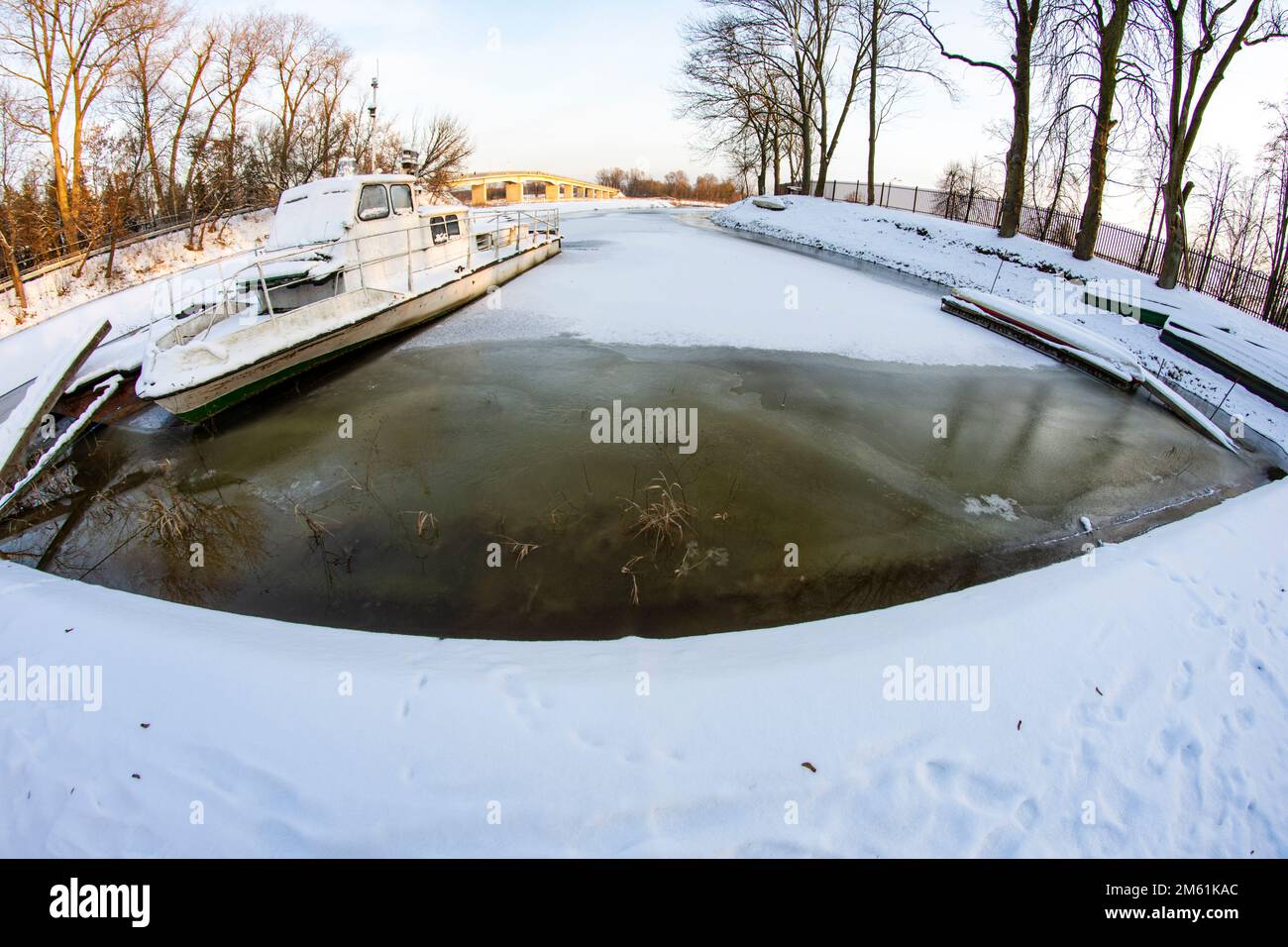 Yacht and jetty in a winter harbor covered in ice and snow, bridge and ...