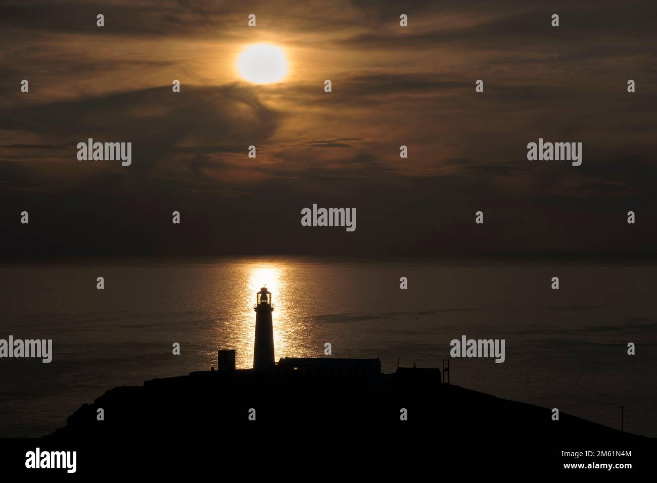 South Stack Lighthouse silhouetted at sunset against the Irish Sea ...