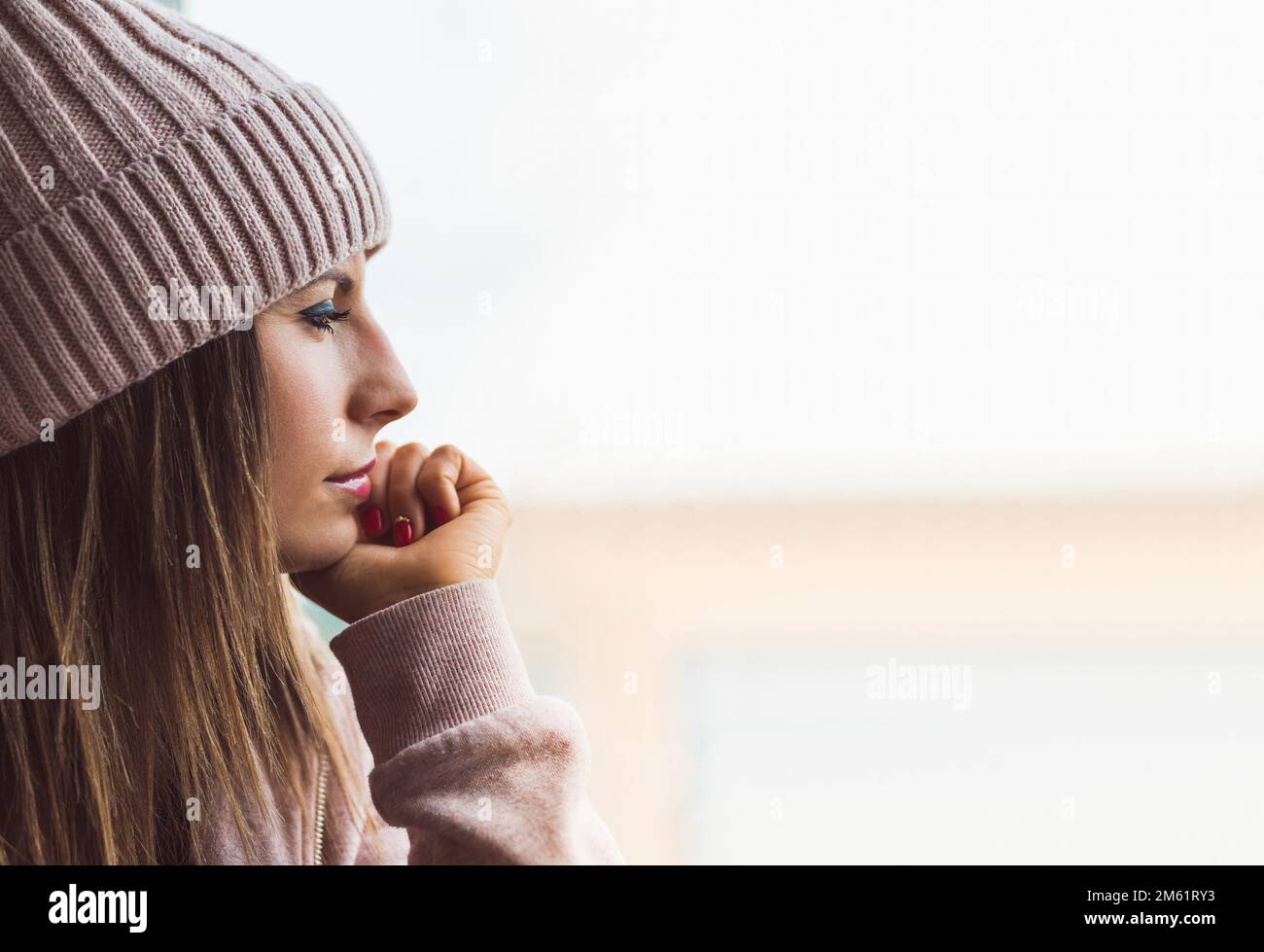 woman in profile wearing a cap and next to a window, looking out ...