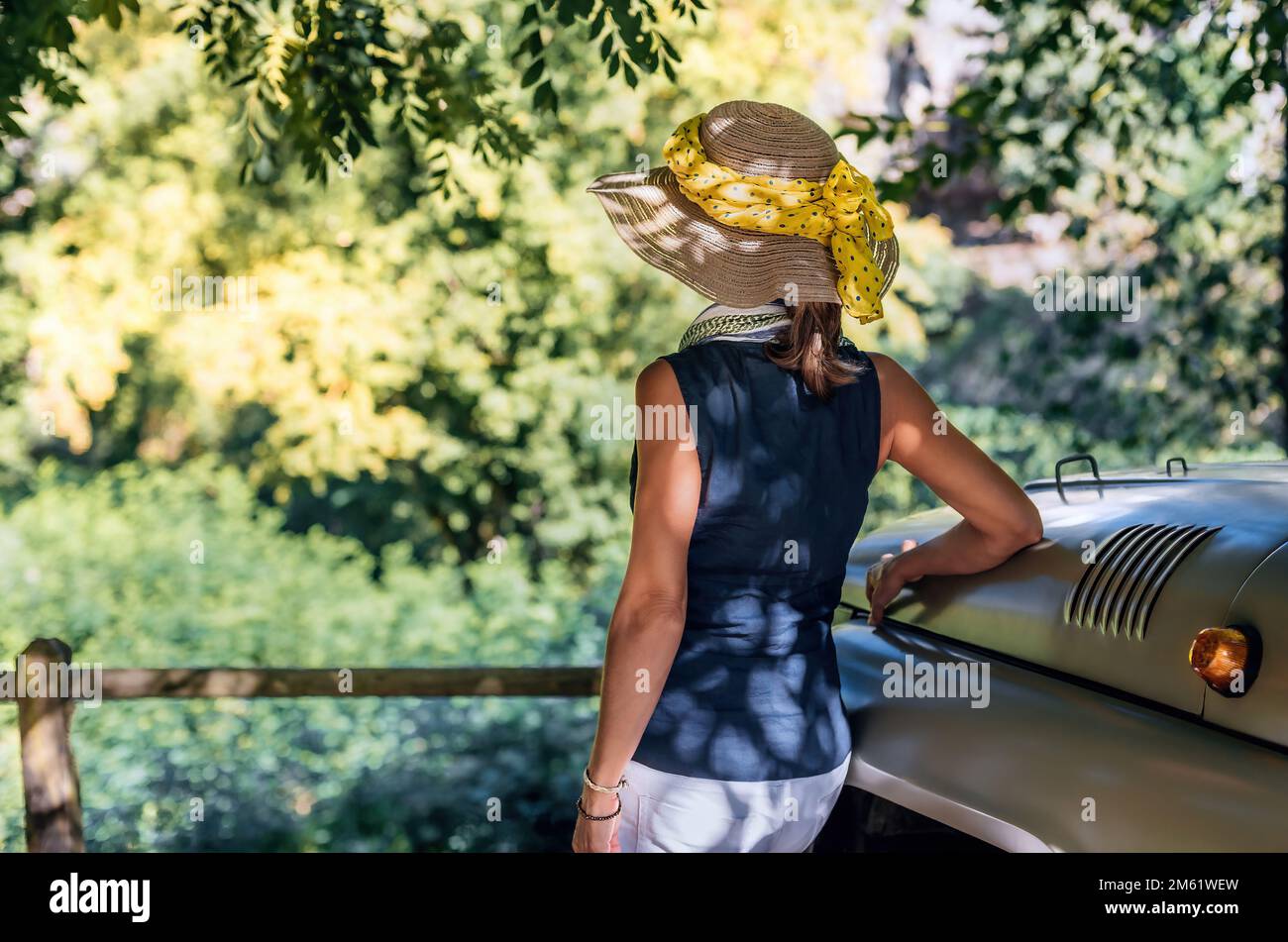 a woman with a hat on her back, leaning on the hood of an SUV looking ...