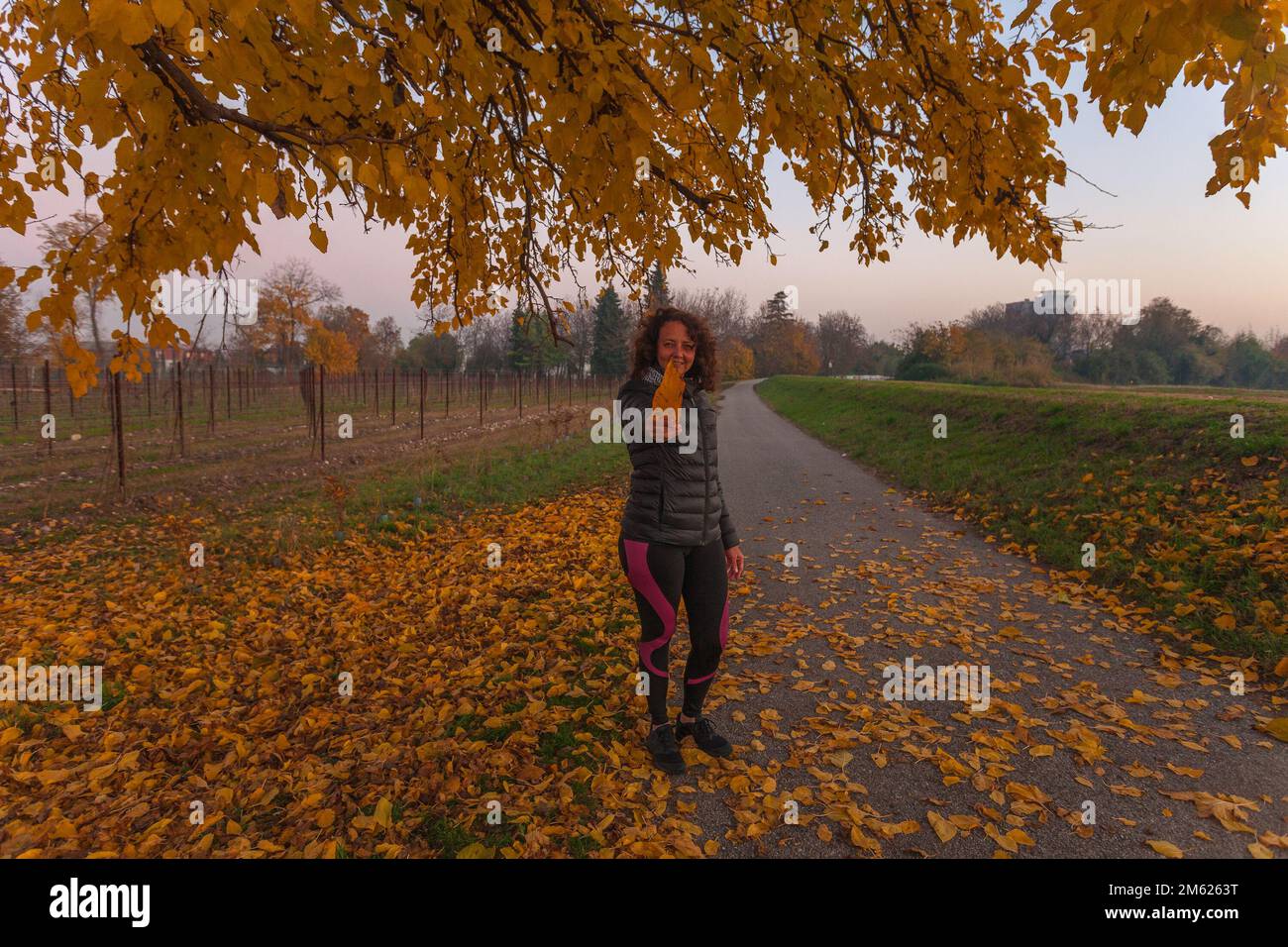 Happy woman under a tree with beautiful autumn colors showing a leaf ...