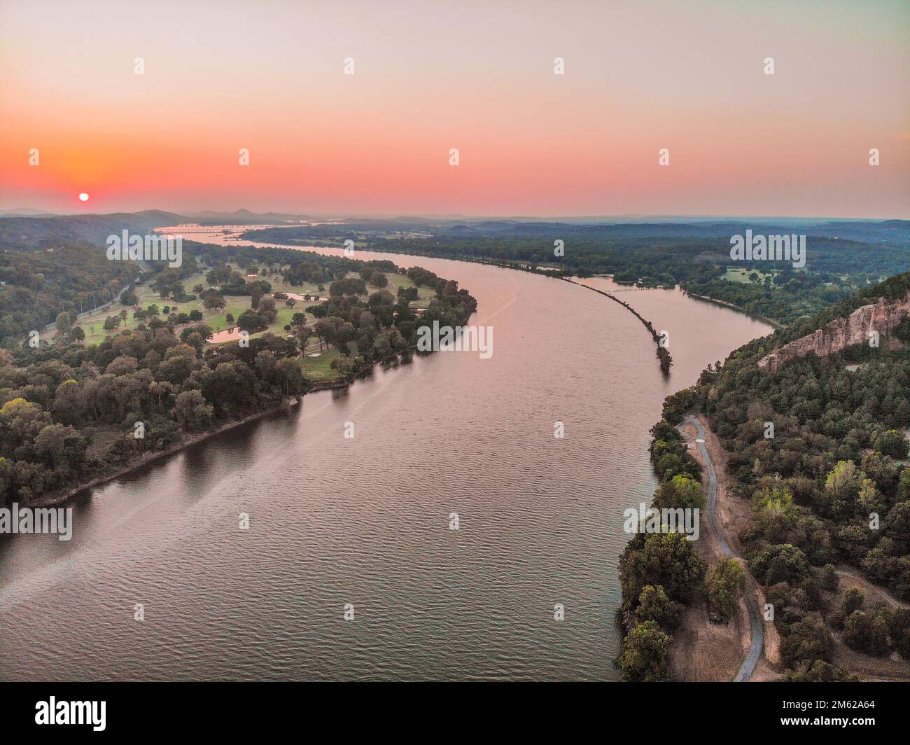 An aerial view of a river surrounded by forested lands under a sunset ...