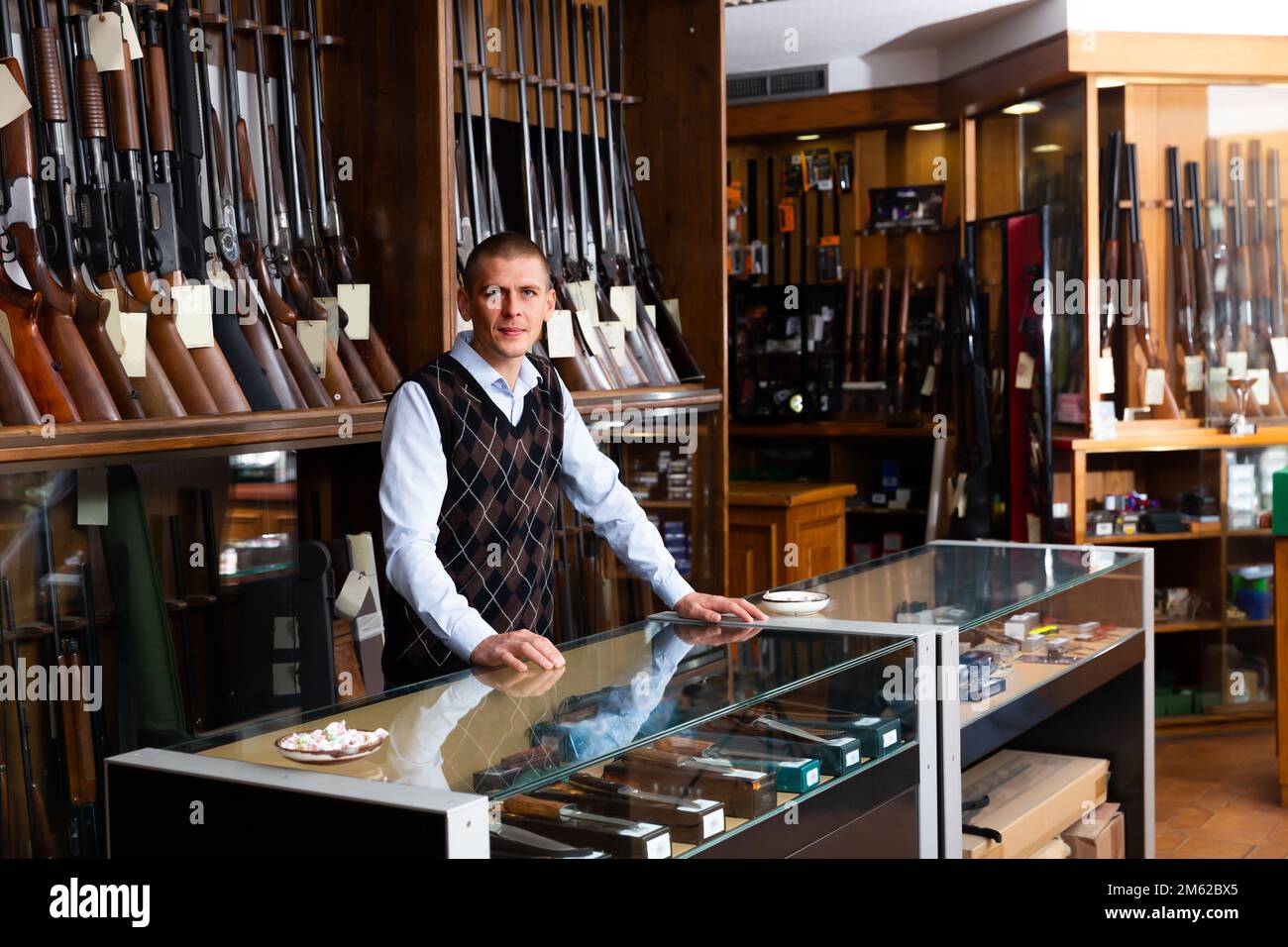 Confident owner of gun shop standing behind counter Stock Photo - Alamy