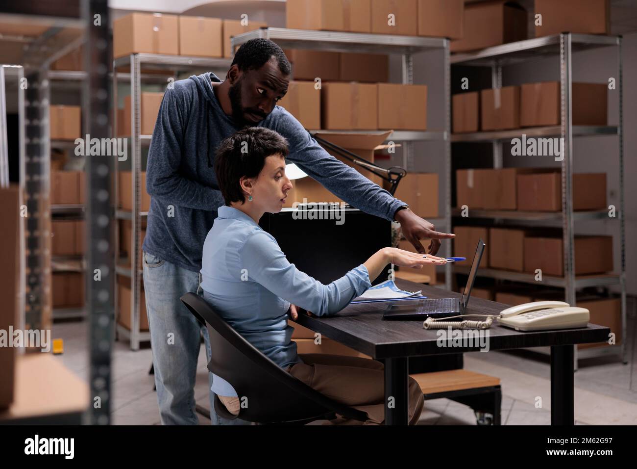 Warehouse employees analyzing delivery checklist on laptop computer searching for metallic box ...