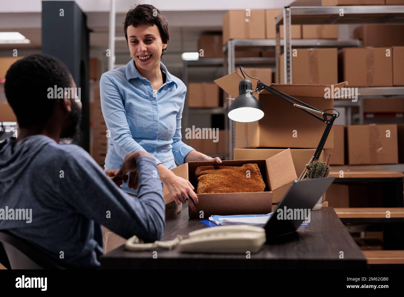 Storehouse worker putting clothes in cardboard box preparing packages ...