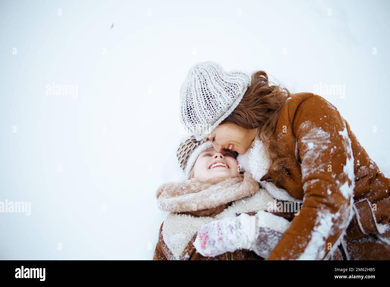 happy modern mother and daughter in coat, hat, scarf and mittens laying ...