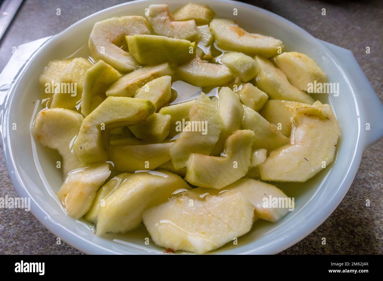 Peeled and sliced apples in a dish of water ready to make apple sauce ...
