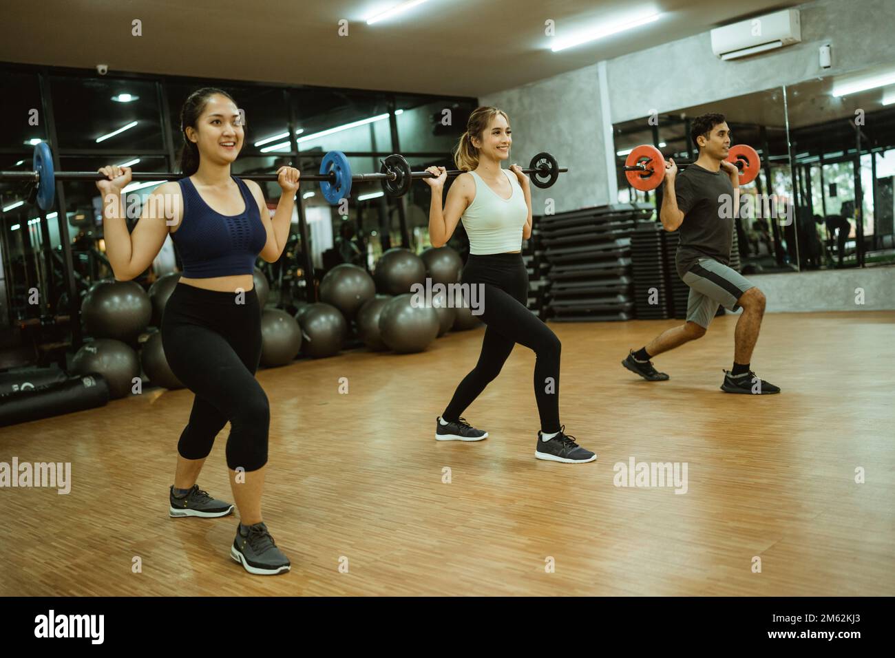 young sporty group doing back squats with barbells during training ...