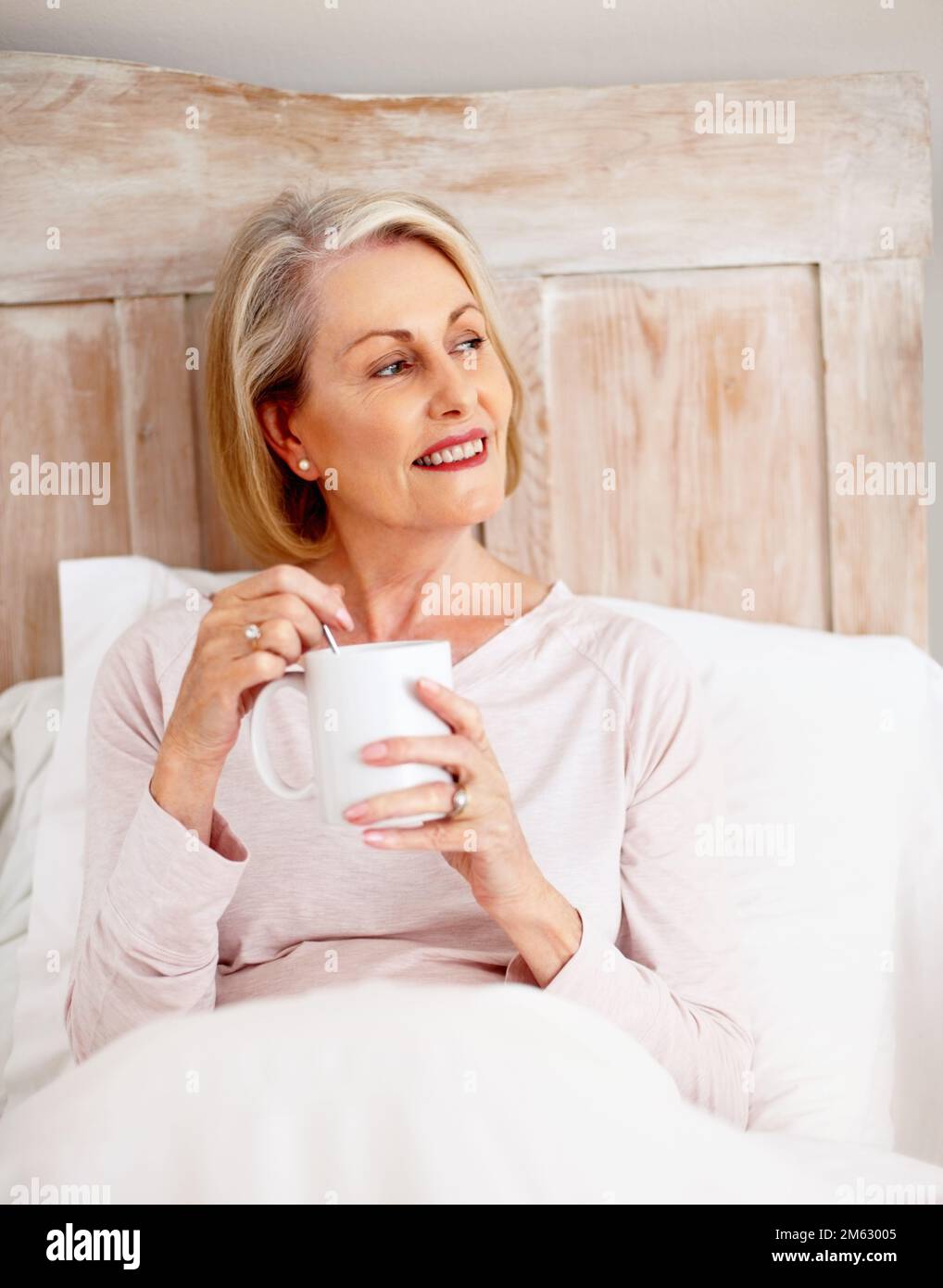 Smiling mature woman holding coffee mug in bed. Portrait of a smiling ...