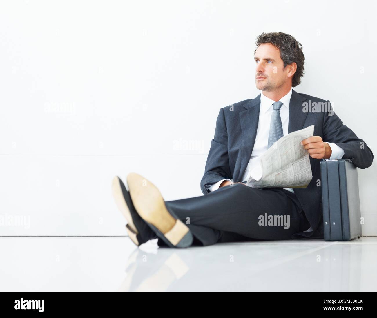 Smart executive sitting against wall with newspaper and briefcase ...