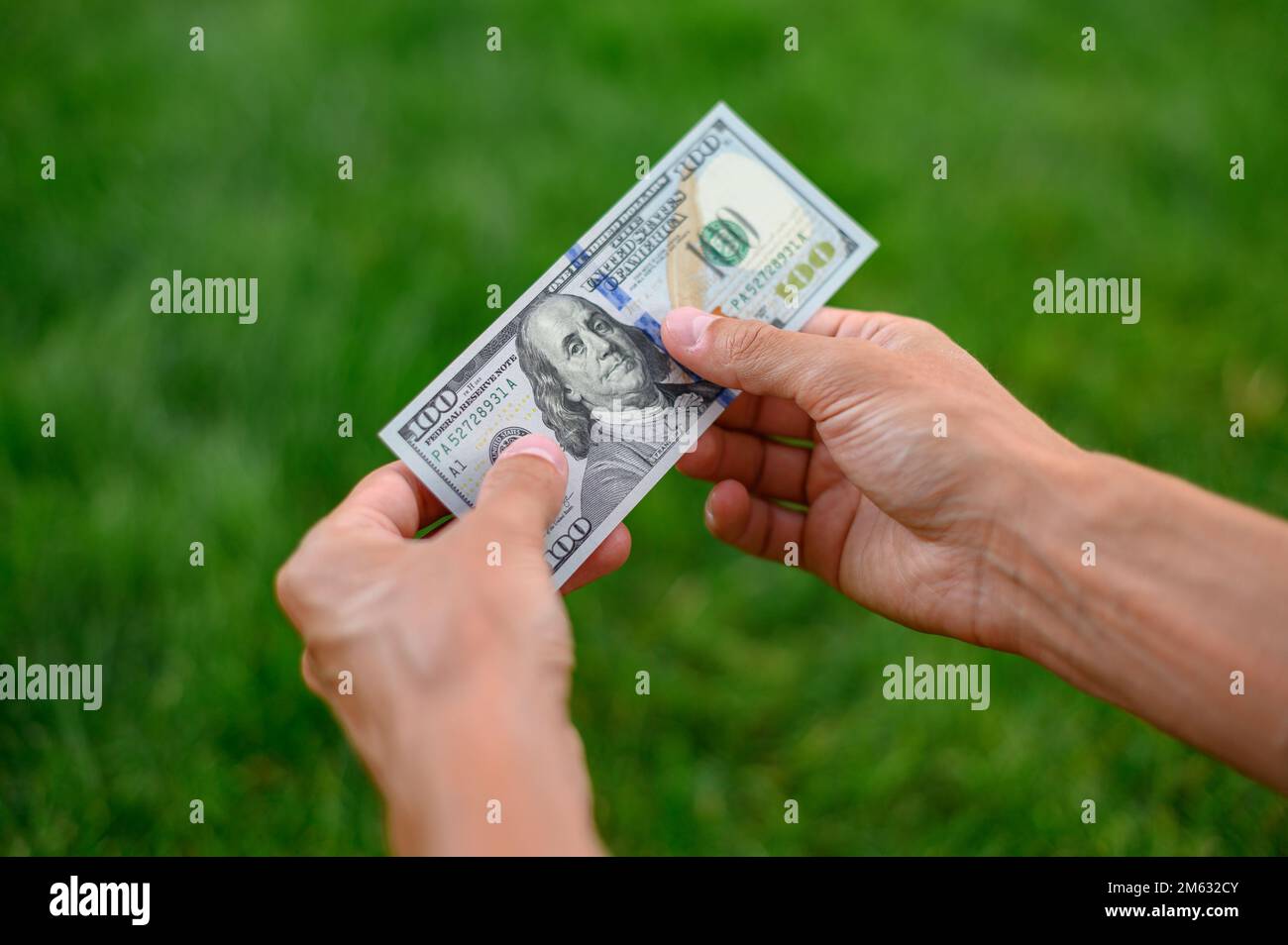 Close up 100 Dollar bank note in hand on grass background. One hundred ...