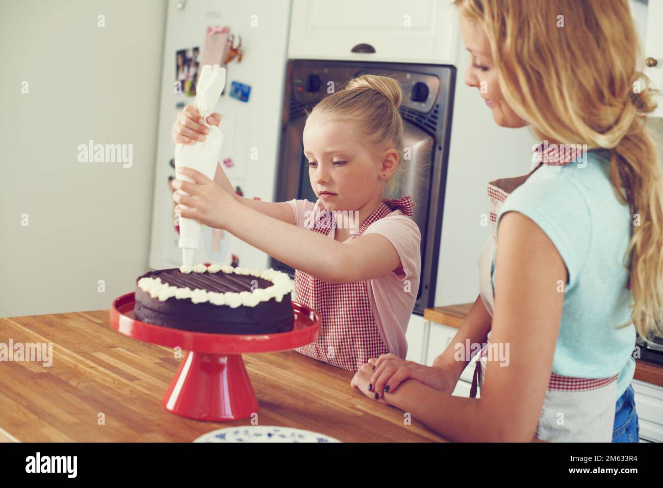 Learning how to ice a cake. Cute little girl icing a cake with her mom ...