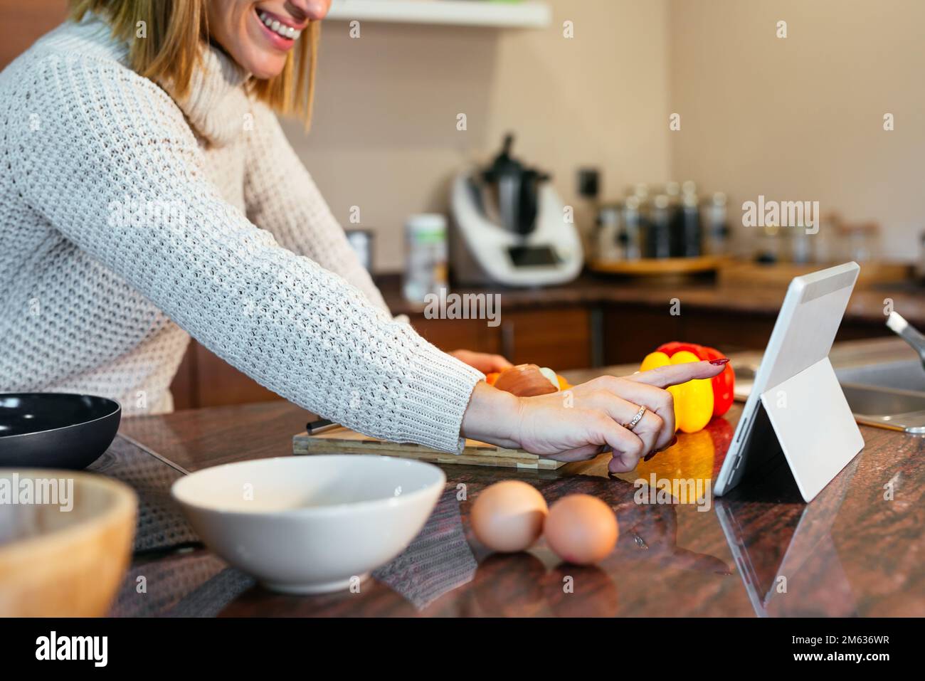 Crop cheerful female in sweater tapping touch screen of tablet ...