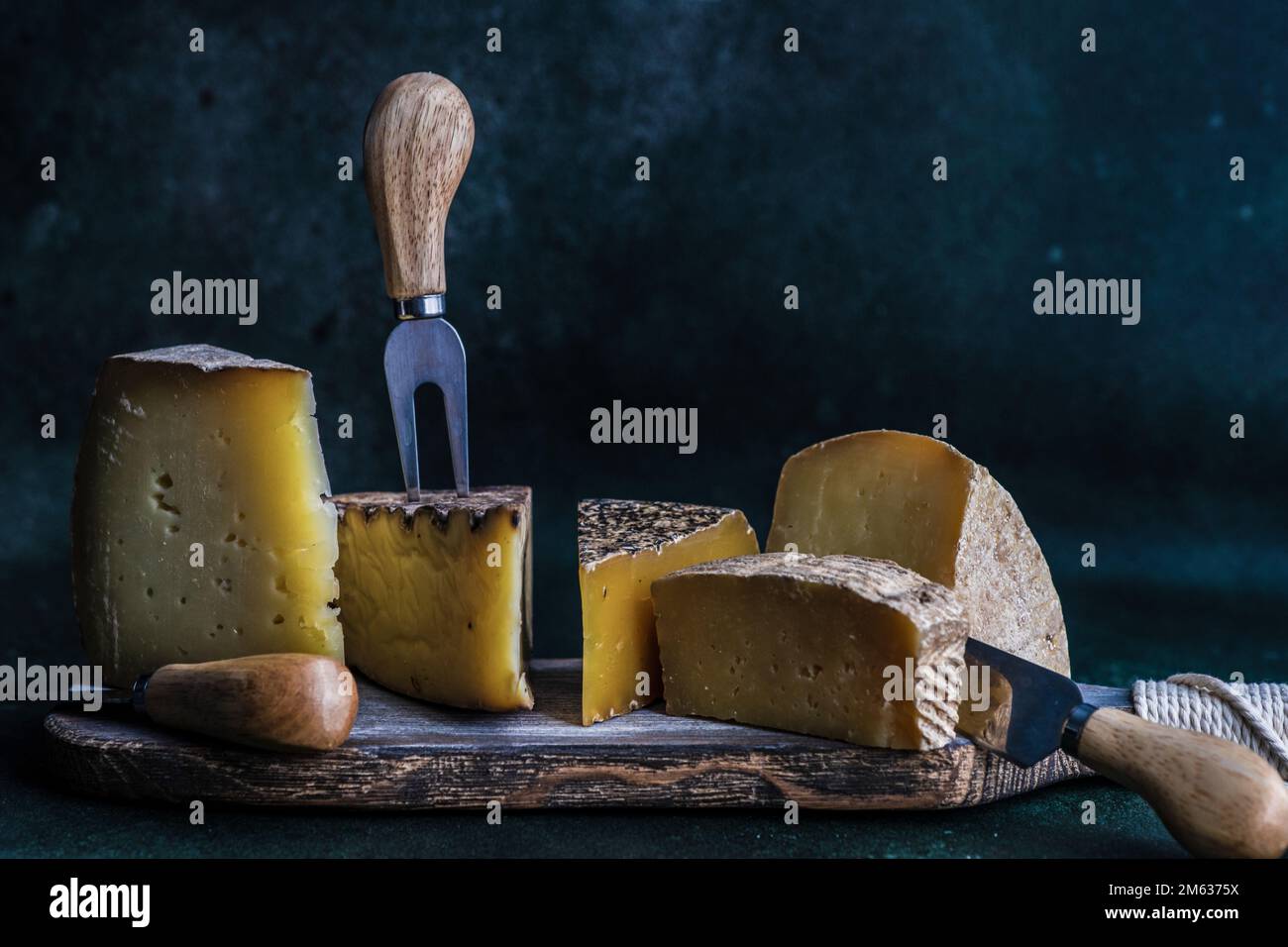 Wooden cutting board with cheese variety on dark concrete background ...