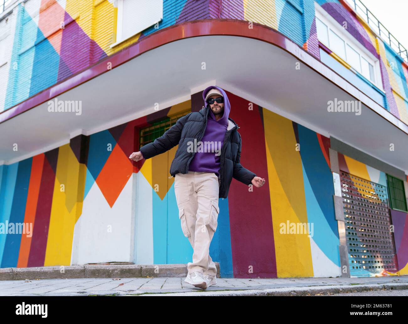 From below full body male dancer in stylish clothes walking on pavement ...