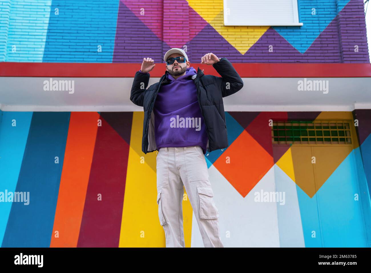 From below male in stylish outerwear raising arms and stretching ...