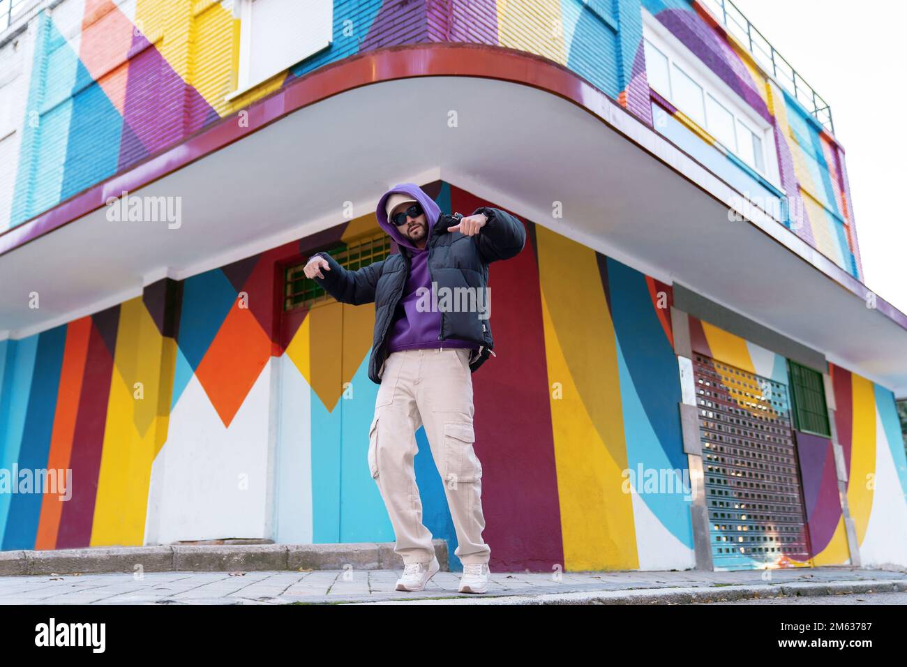 From below full body male dancer in stylish clothes walking on pavement ...