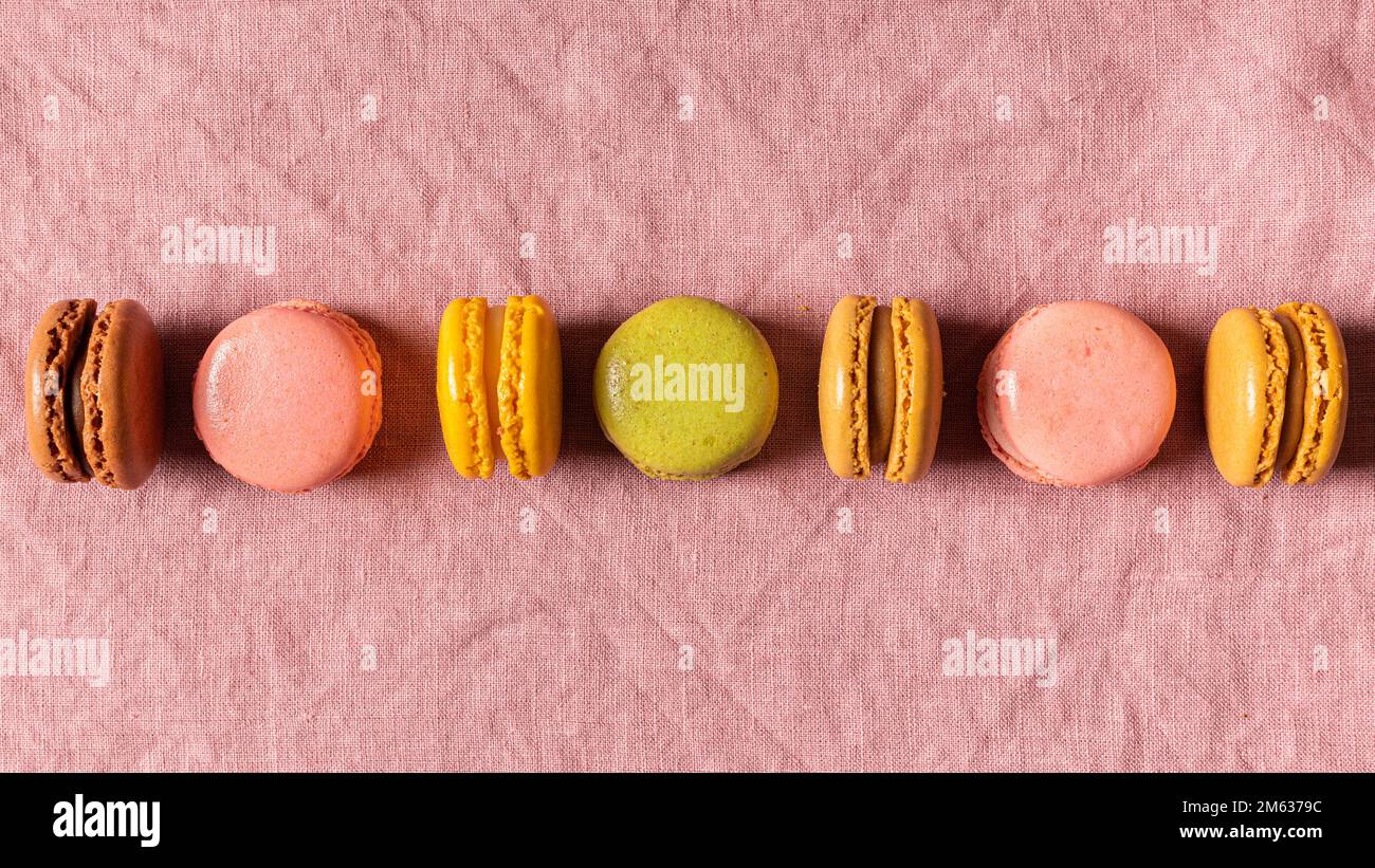 Top view of even row of composed multicolored French macaroons on pink ...