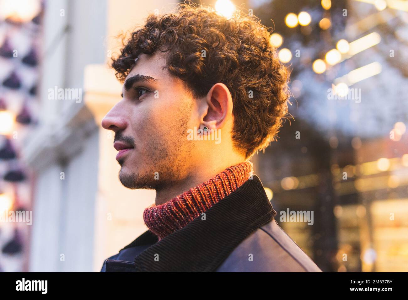 Hispanic male with curly hair in black jacket looking away against ...