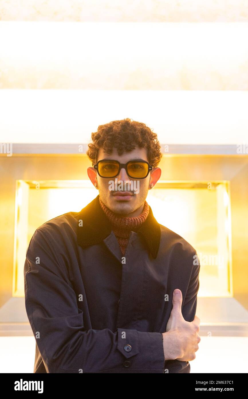 Curly ethnic guy in trendy eyeglasses looking at camera while standing ...