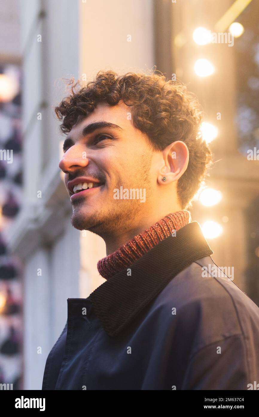 Hispanic male with curly hair in black jacket looking away with smile ...