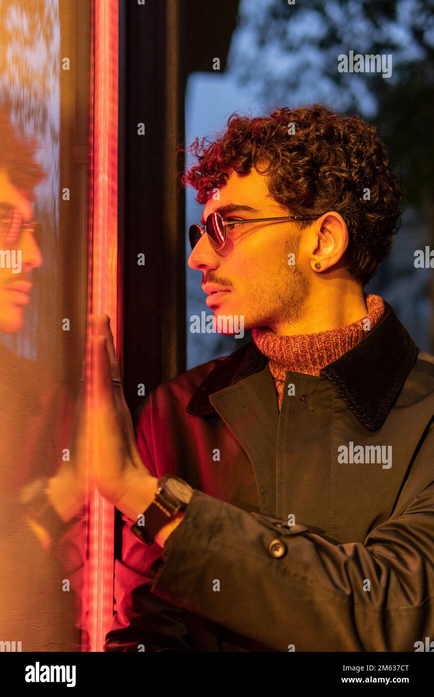 Pondering ethnic guy with curly hair in round glasses looking out ...