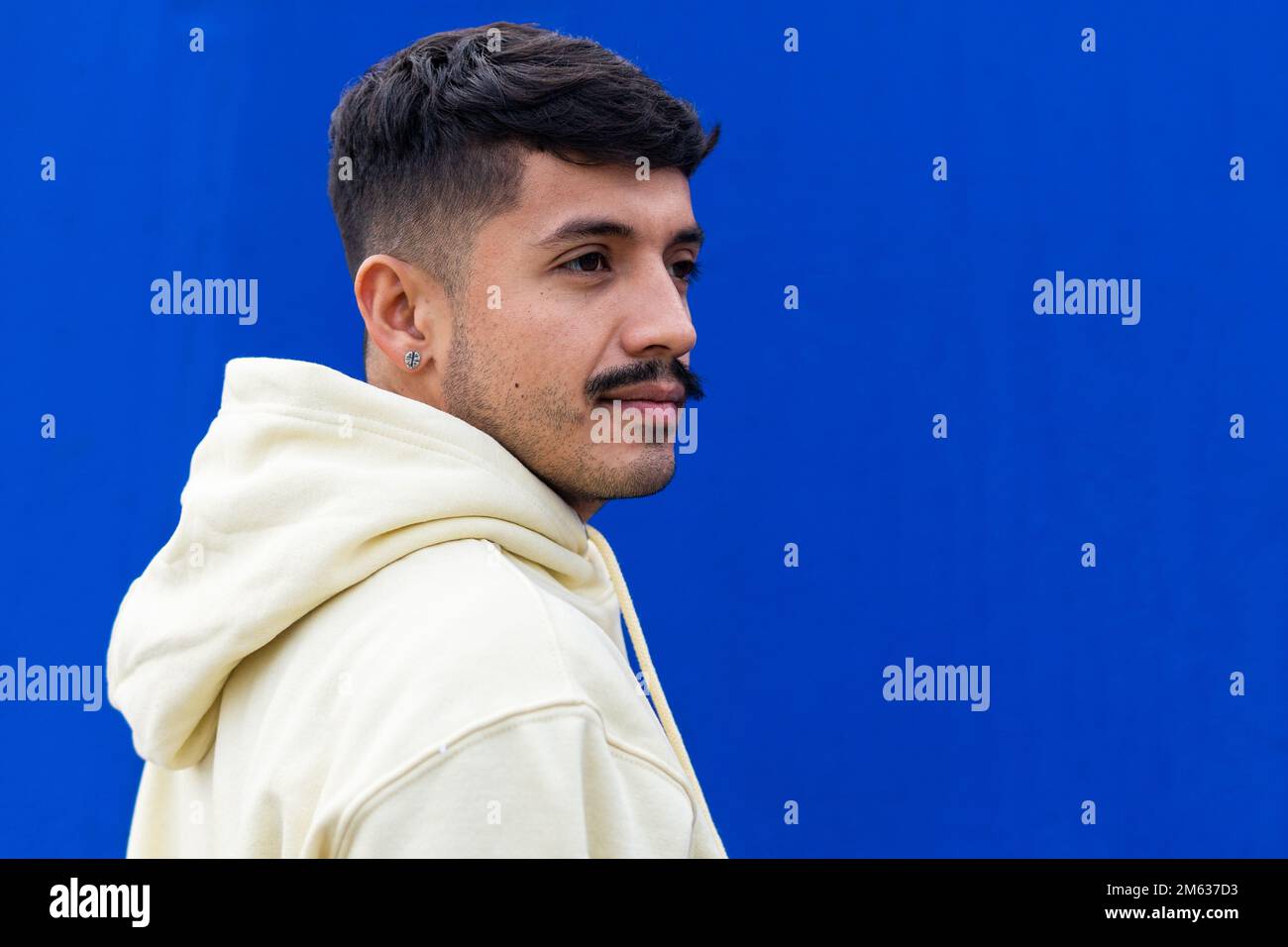 Young Hispanic male in white hoodie and mustache looking away against ...