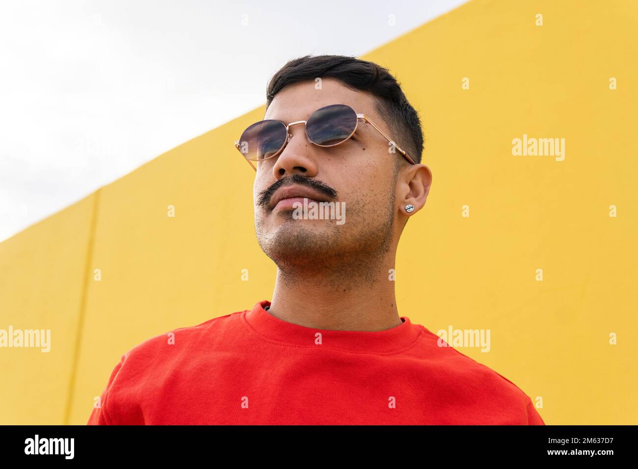 From below young Hispanic male in red sweatshirt in stylish sunglasses ...