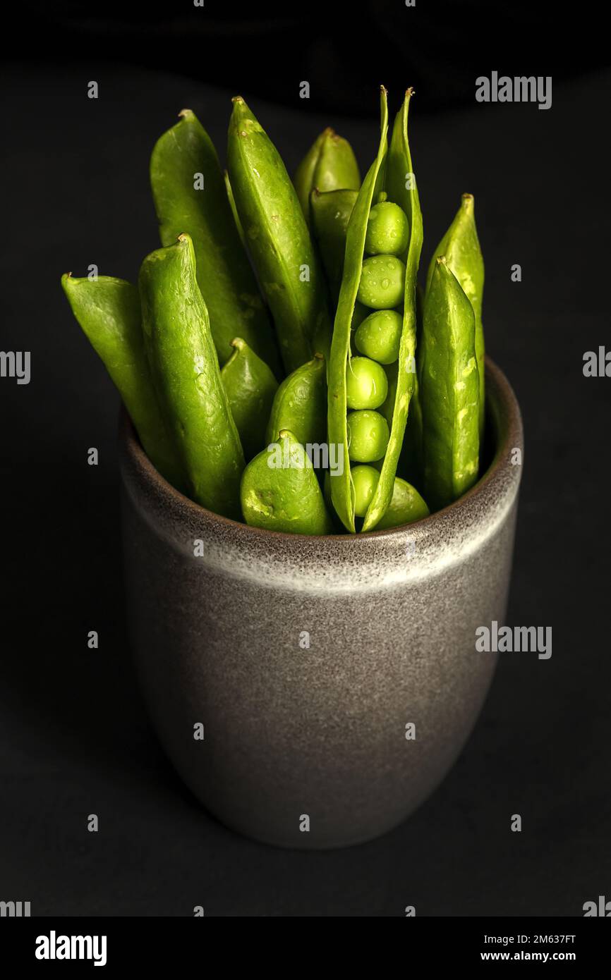 Bunch of ripe green pods with fresh peas placed in ceramic pot against ...