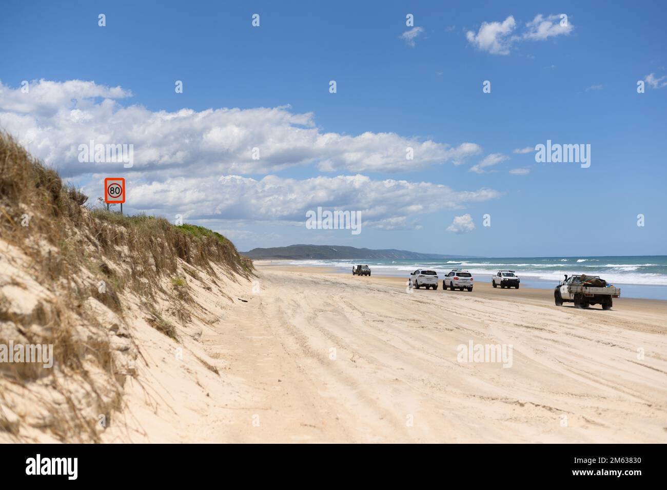 Modern automobiles driving on sandy coast near waving ocean under blue ...