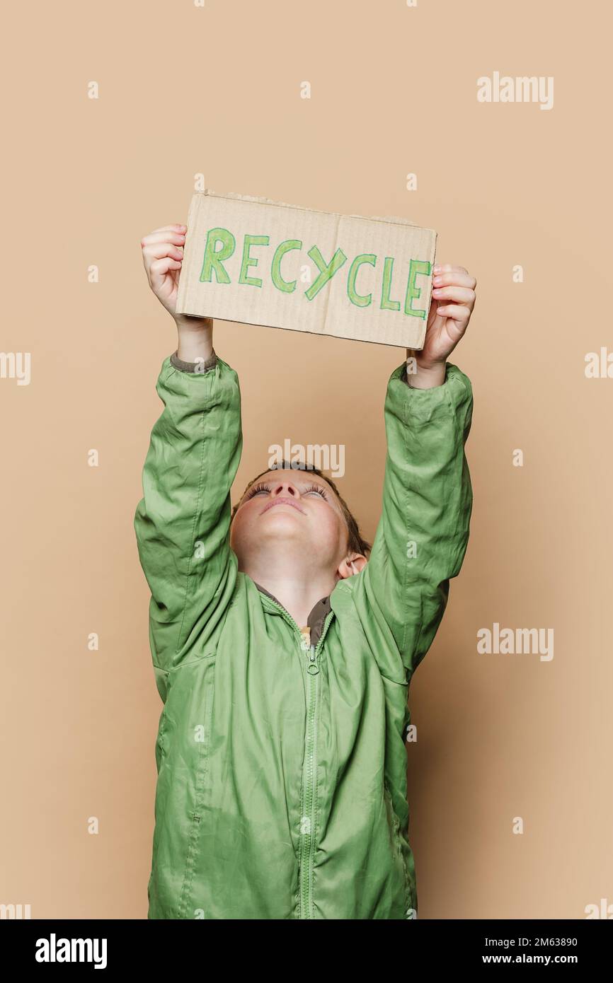 Boy in green outerwear raising arms with Recycle poster and looking up ...