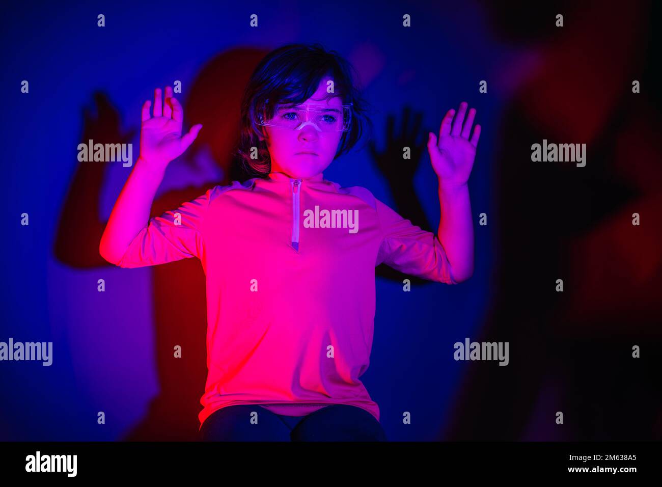 Kid in smart goggles with hands raised standing in dark room ...