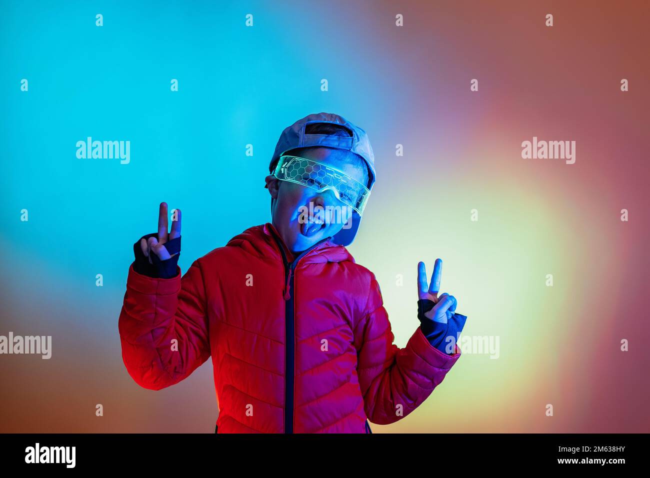 Cheerful boy in outerwear cap and smart goggles showing tongue and two ...