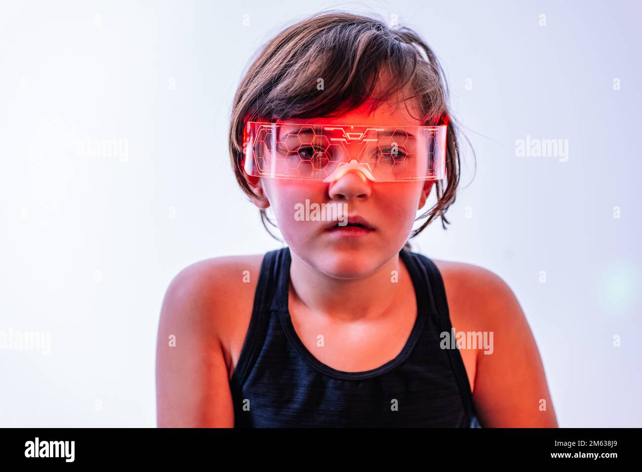 Thoughtful kid in orange smart goggles exploring virtual reality ...