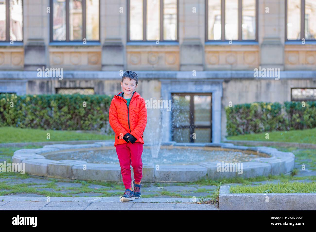 Full body happy boy in red outerwear smiling and looking at camera ...