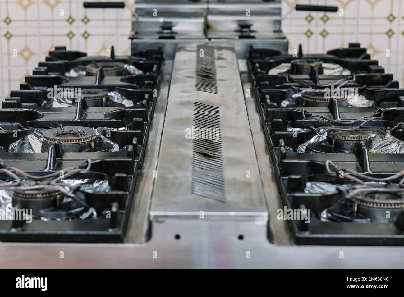 High angle rows of gas stoves separated by metal hood fan placed in ...