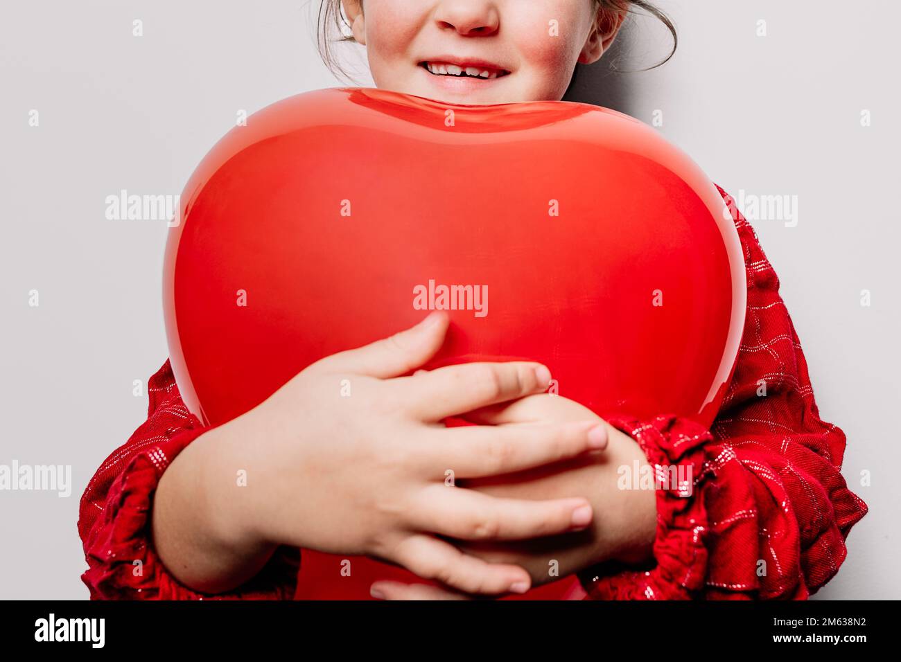 Cropped unrecognizable cute smiling girl in red dress embracing heart ...
