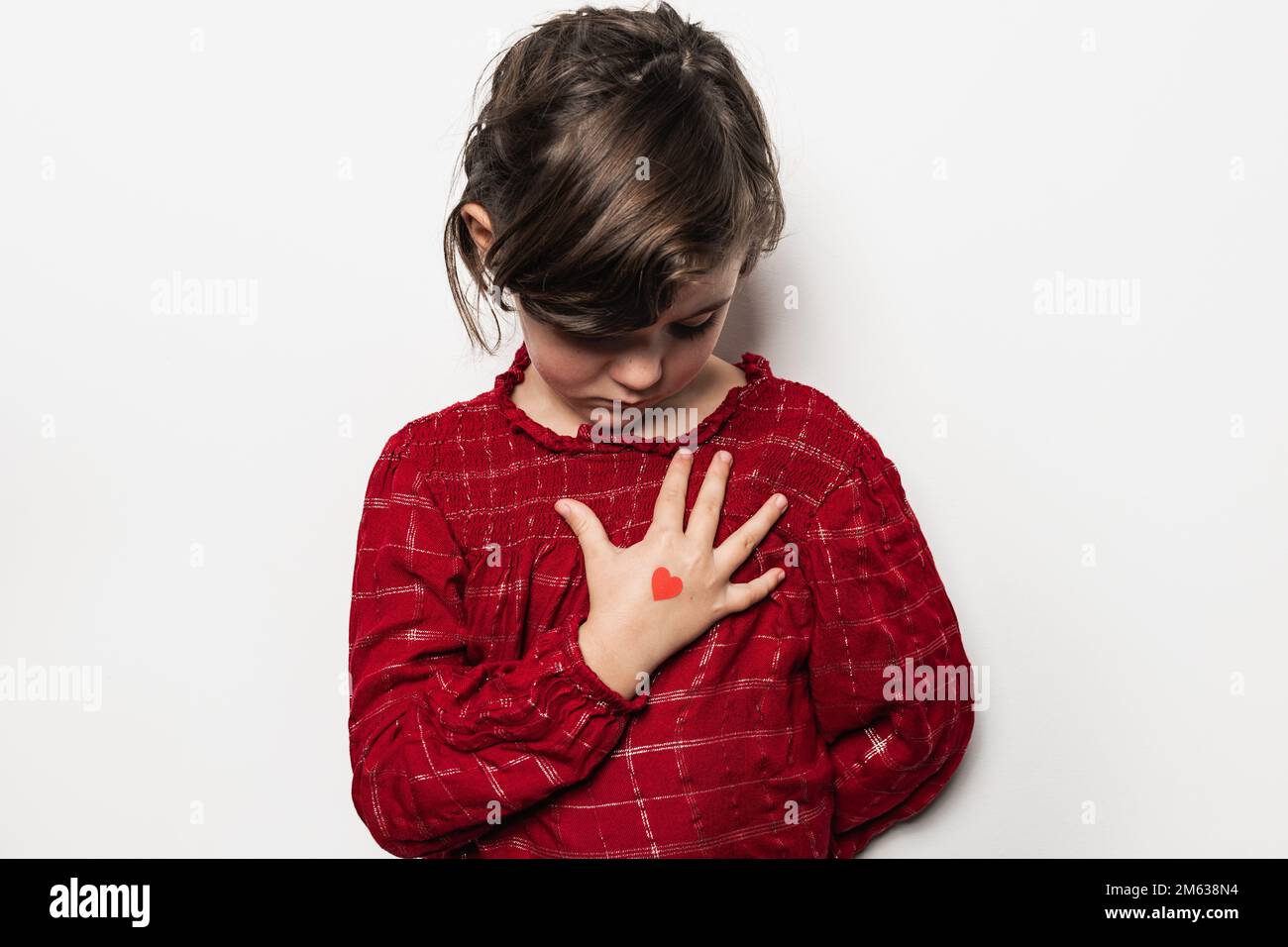 Cute girl with small heart on hand touching chest and looking down ...