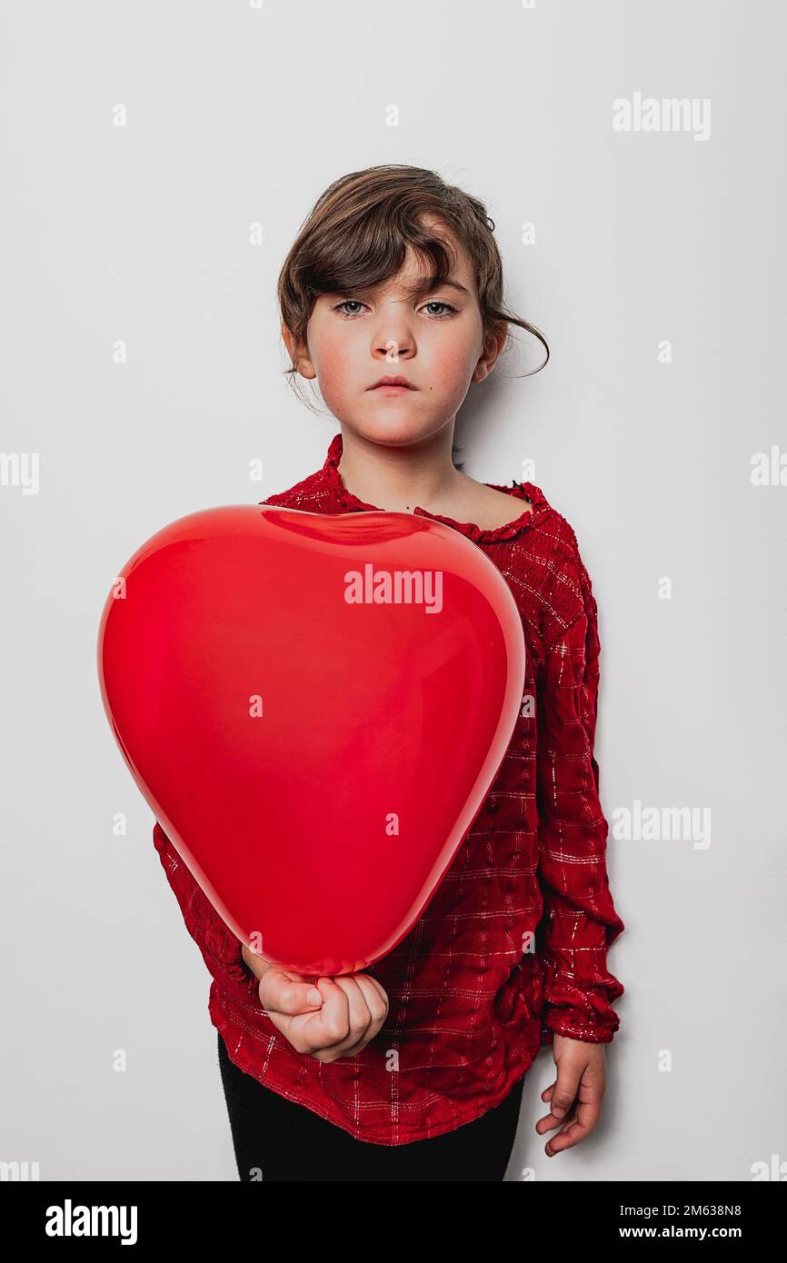 Serious girl showing heart shaped balloon of red color and looking at ...