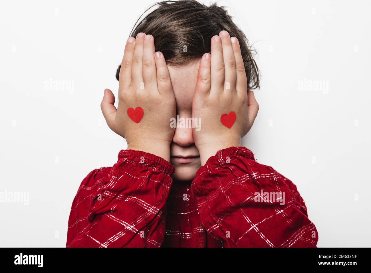 Adorable unrecognizable girl with small hearts on hands covering eyes ...