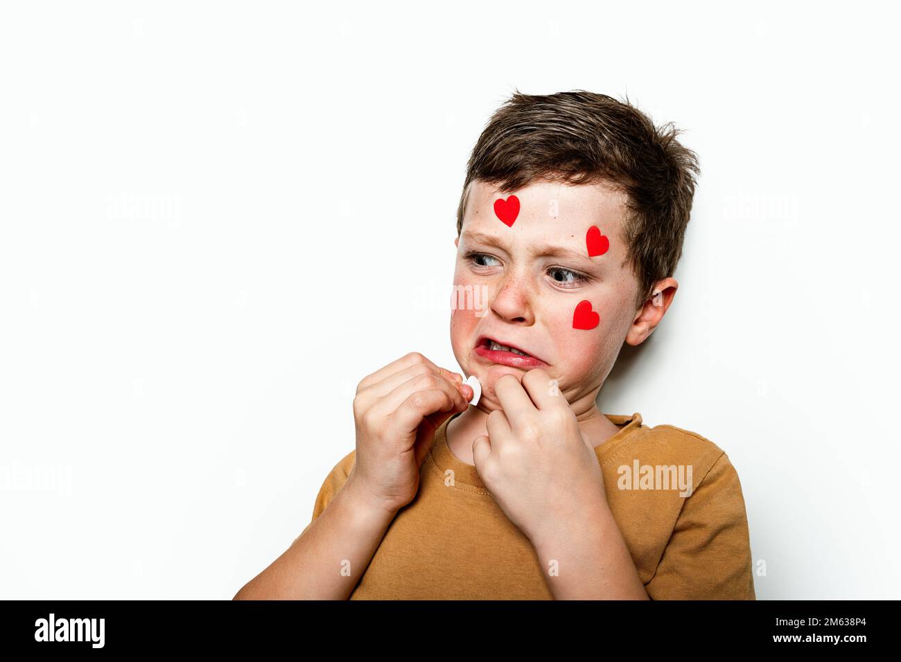 Funny boy grimacing and removing heart shaped stickers from face and ...